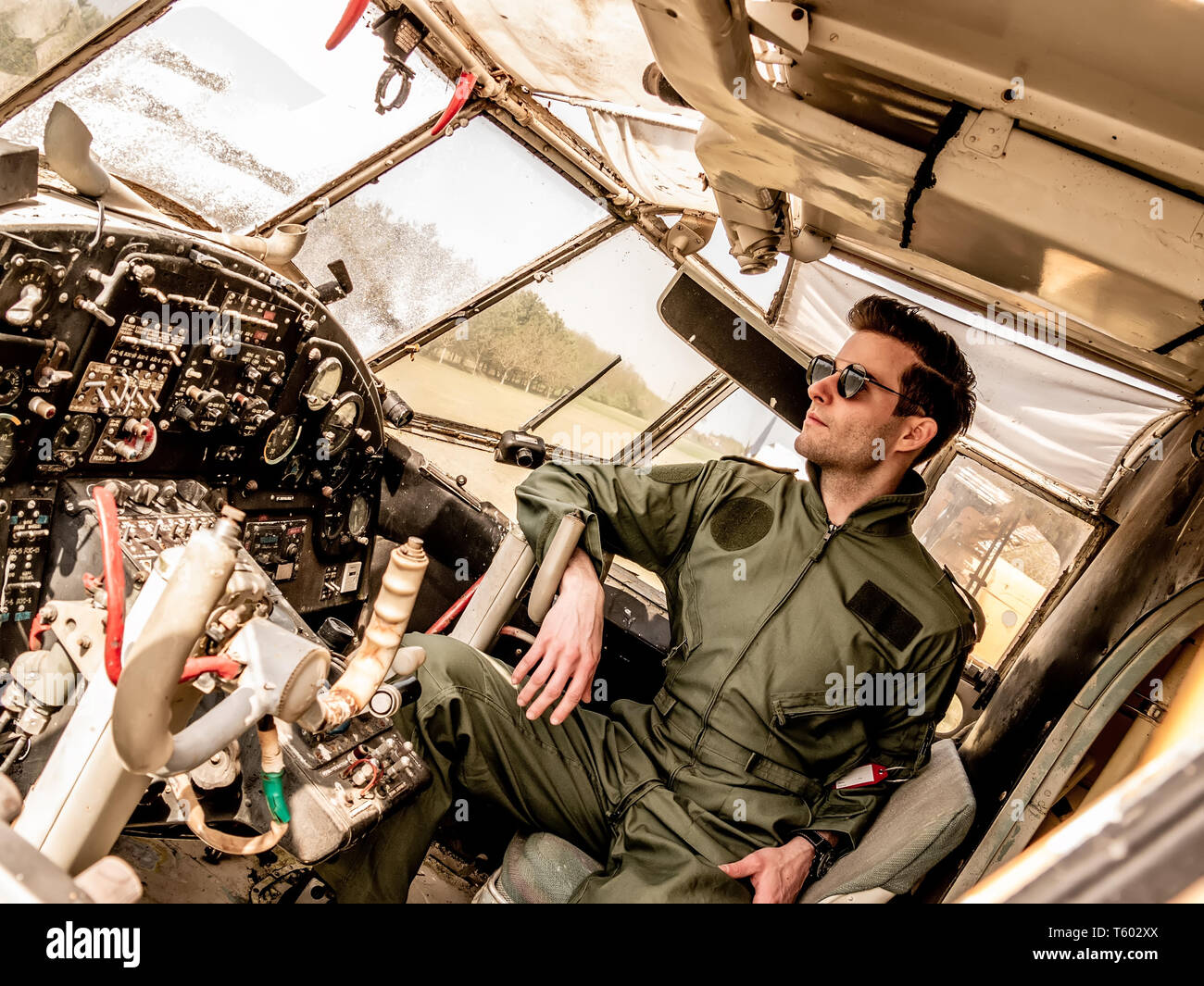 A handsome young man pilot in a green overall sitting in the cockpit of ...