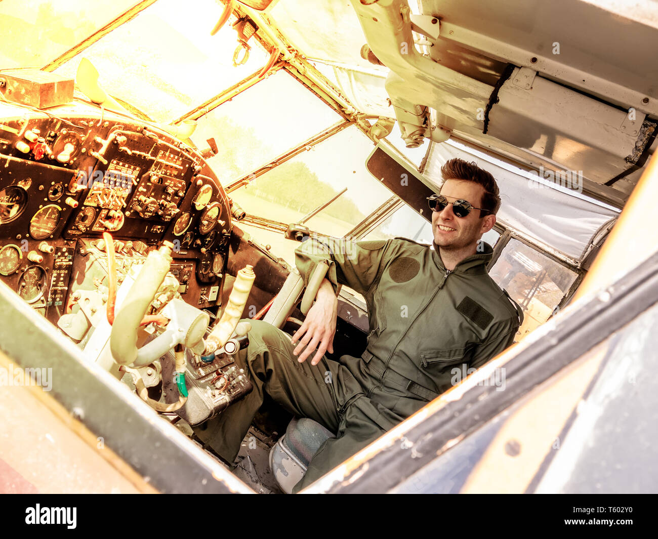 A handsome young man pilot in a green overall sitting in the cockpit of ...