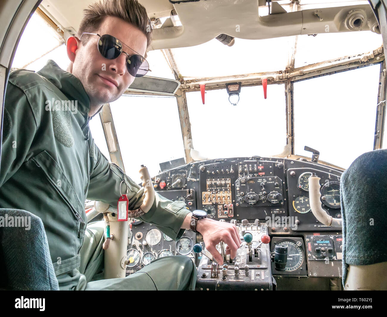 A handsome young man pilot in a green overall sitting in the cockpit of ...