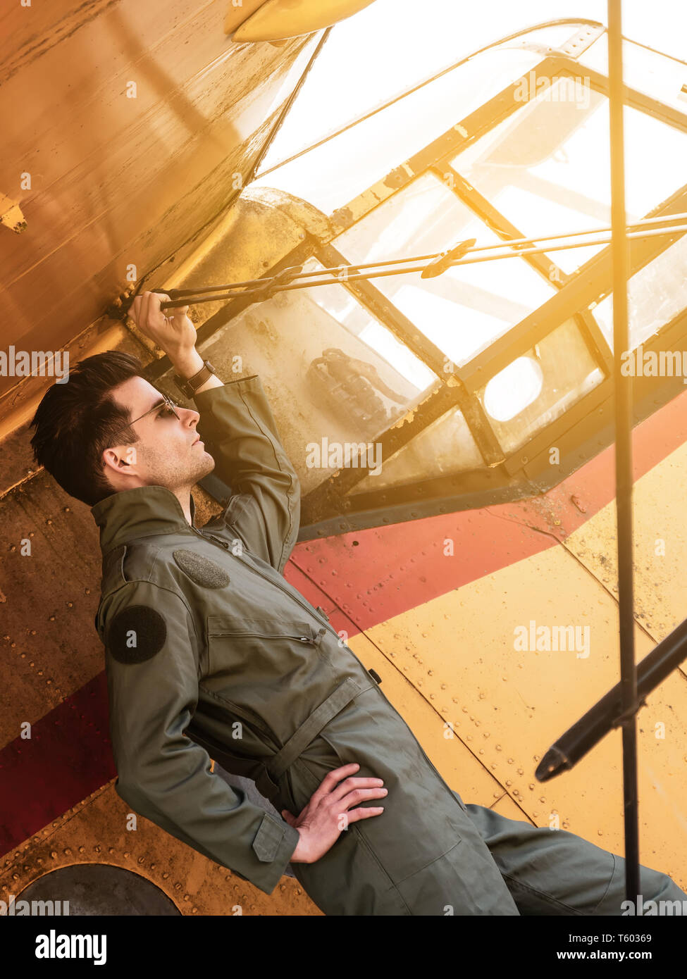 A handsome young man pilot in a green overall standing on the wing of ...