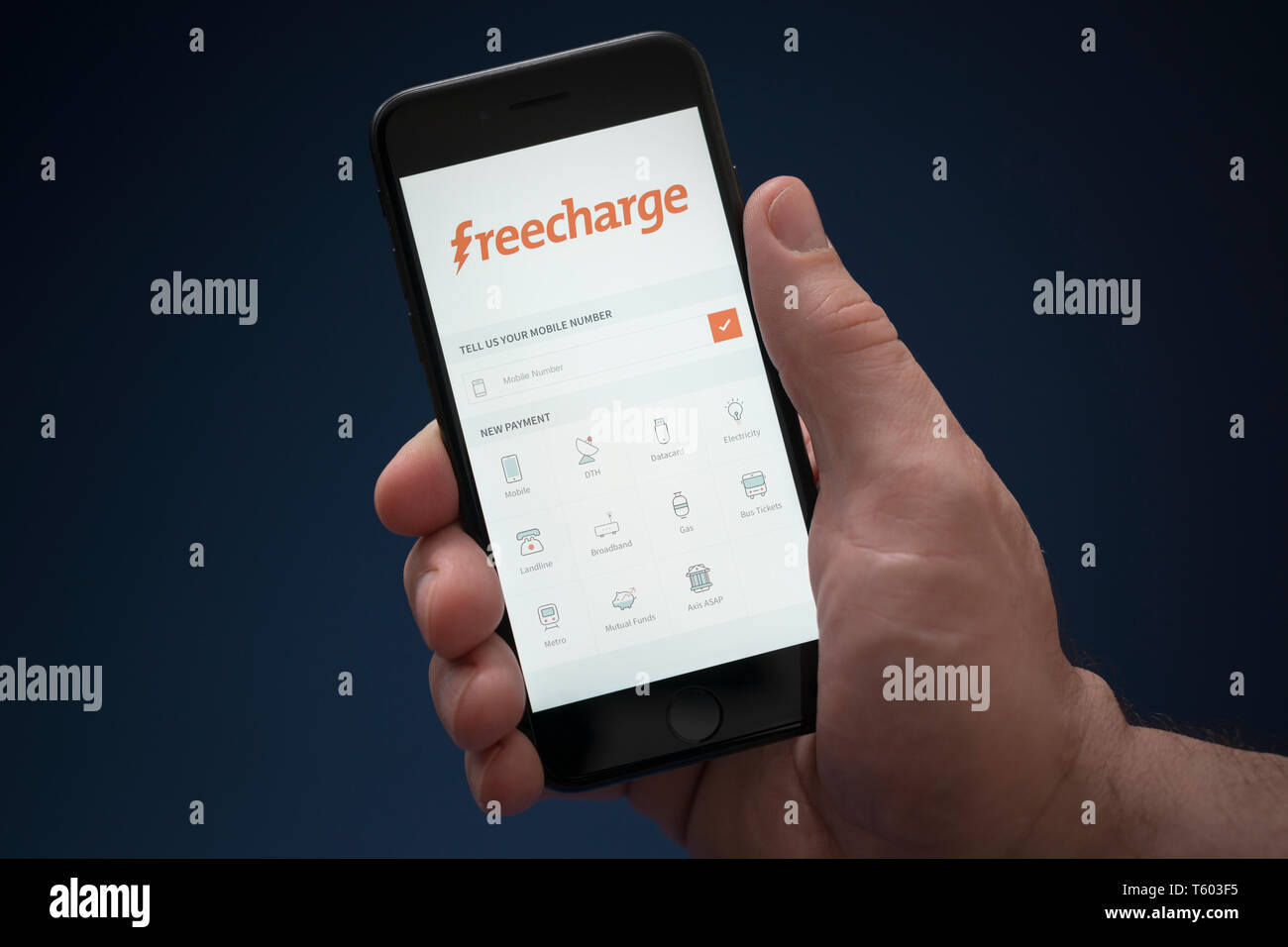 A man looks at his iPhone which displays the Freecharge logo (Editorial ...