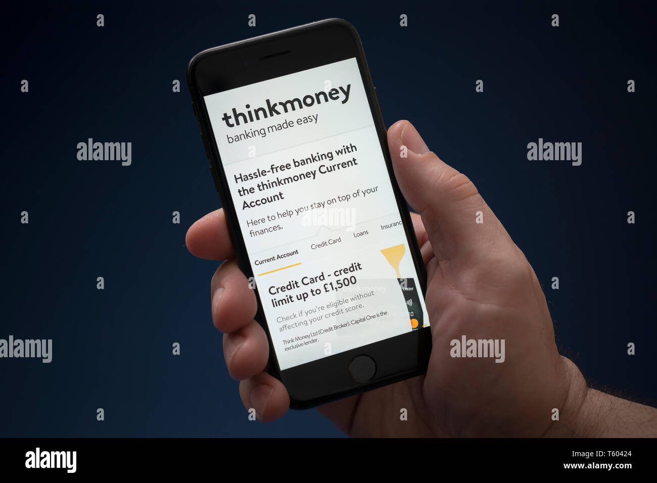 A man looks at his iPhone which displays the Thinkmoney logo (Editorial ...