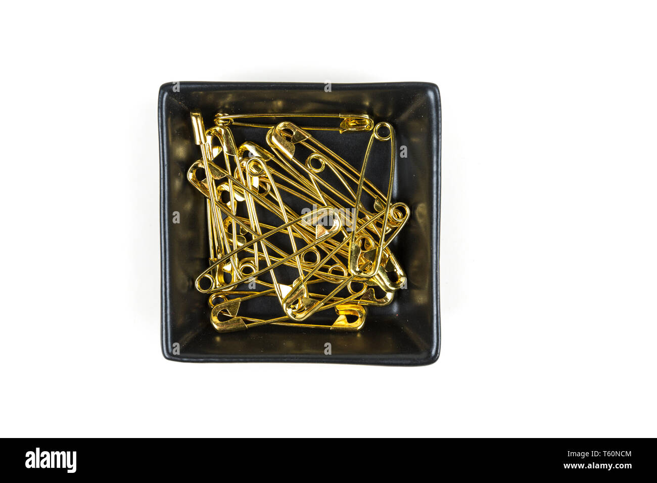 Black dish of gold colored safety pins on a white background Stock ...