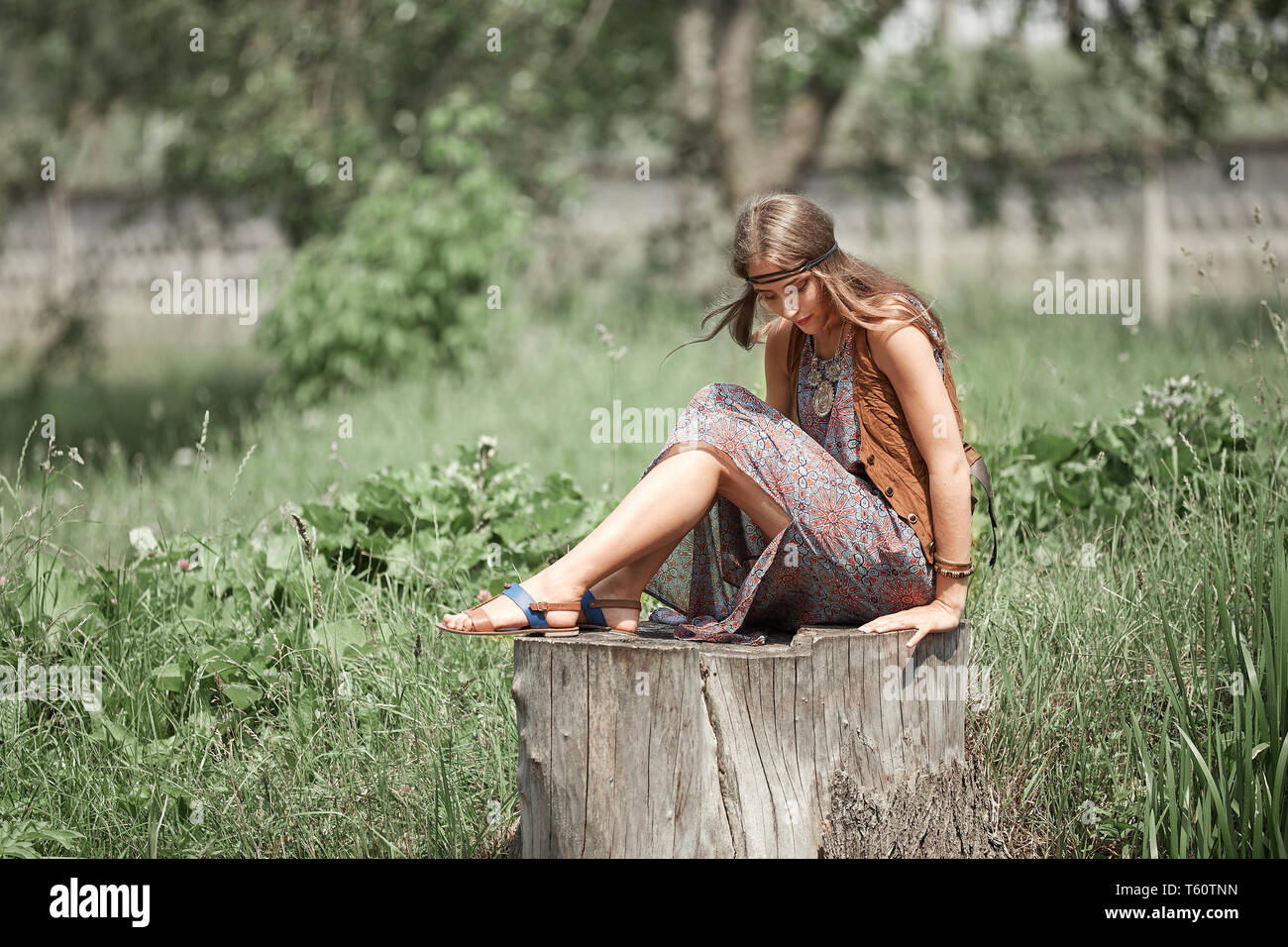 dreaming hippie girl sitting on a big stump in a city Park. the concept of unity with nature ...