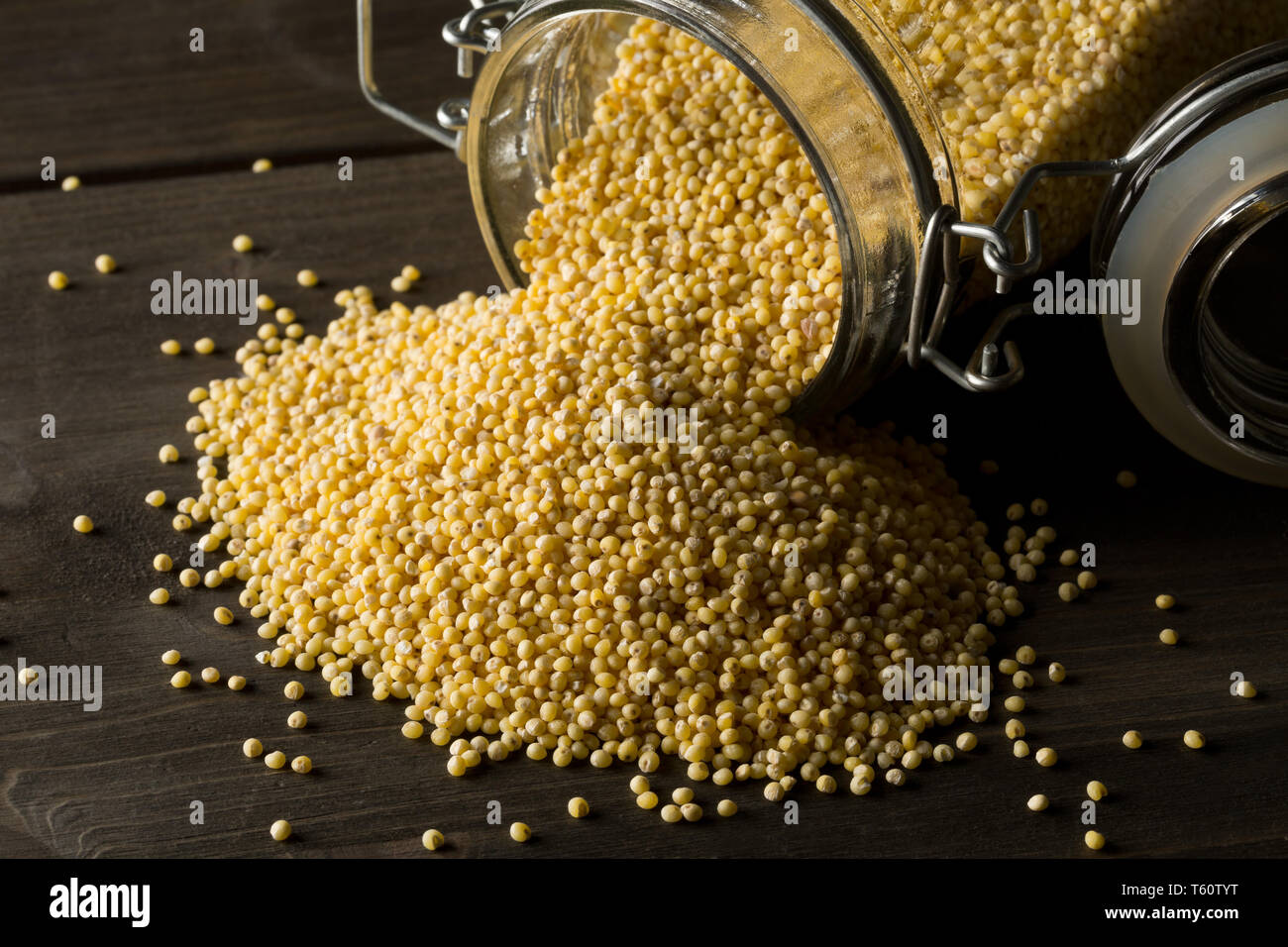 Pile of golden millet, a gluten free grain seed, in glass storage jar ...