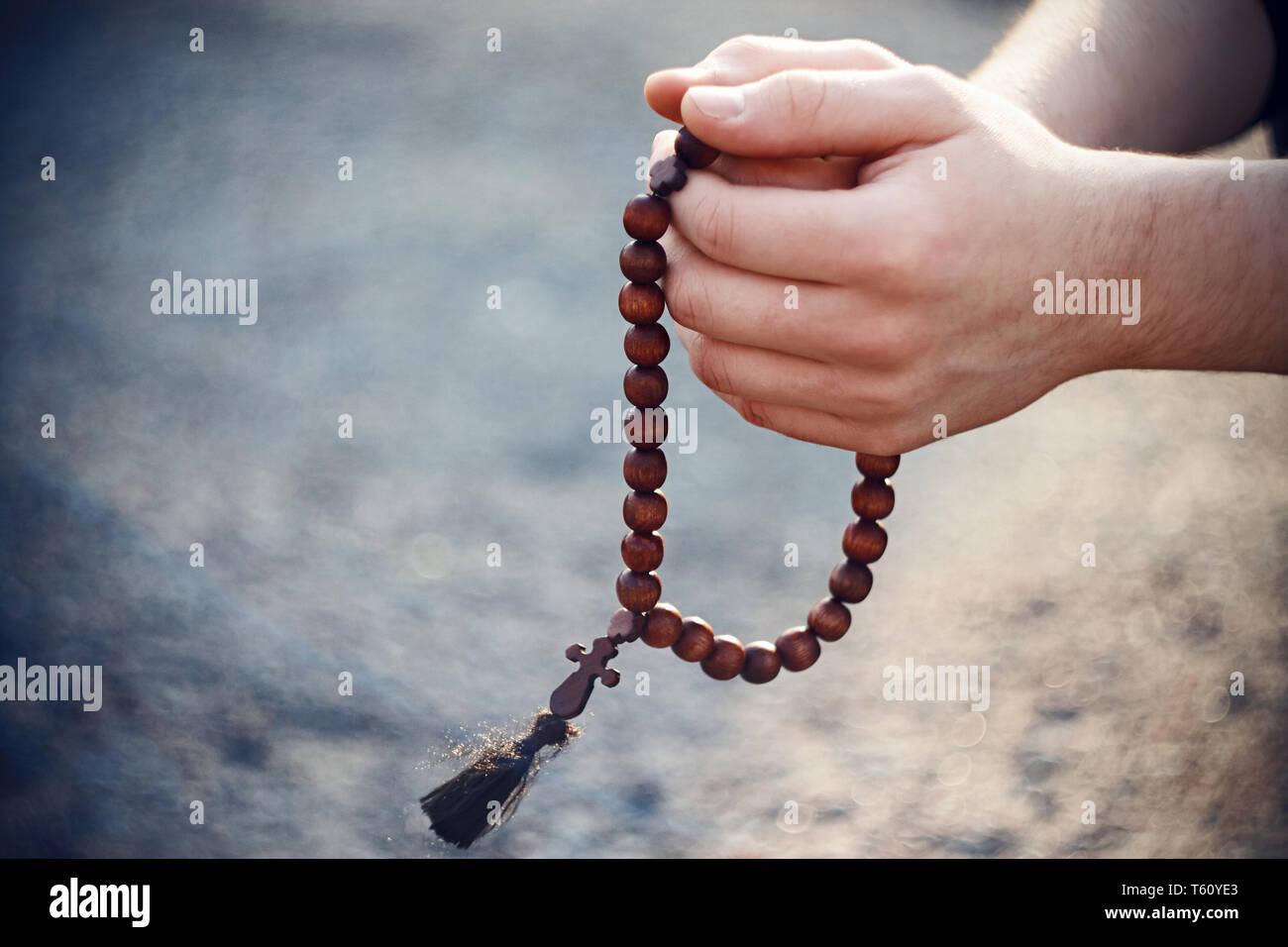 Man holding a wooden rosary and praying. Hands with rosary illuminated ...