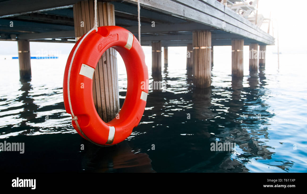Closeup photo of red saving ring hanging wooden pier. Safety on sea ...