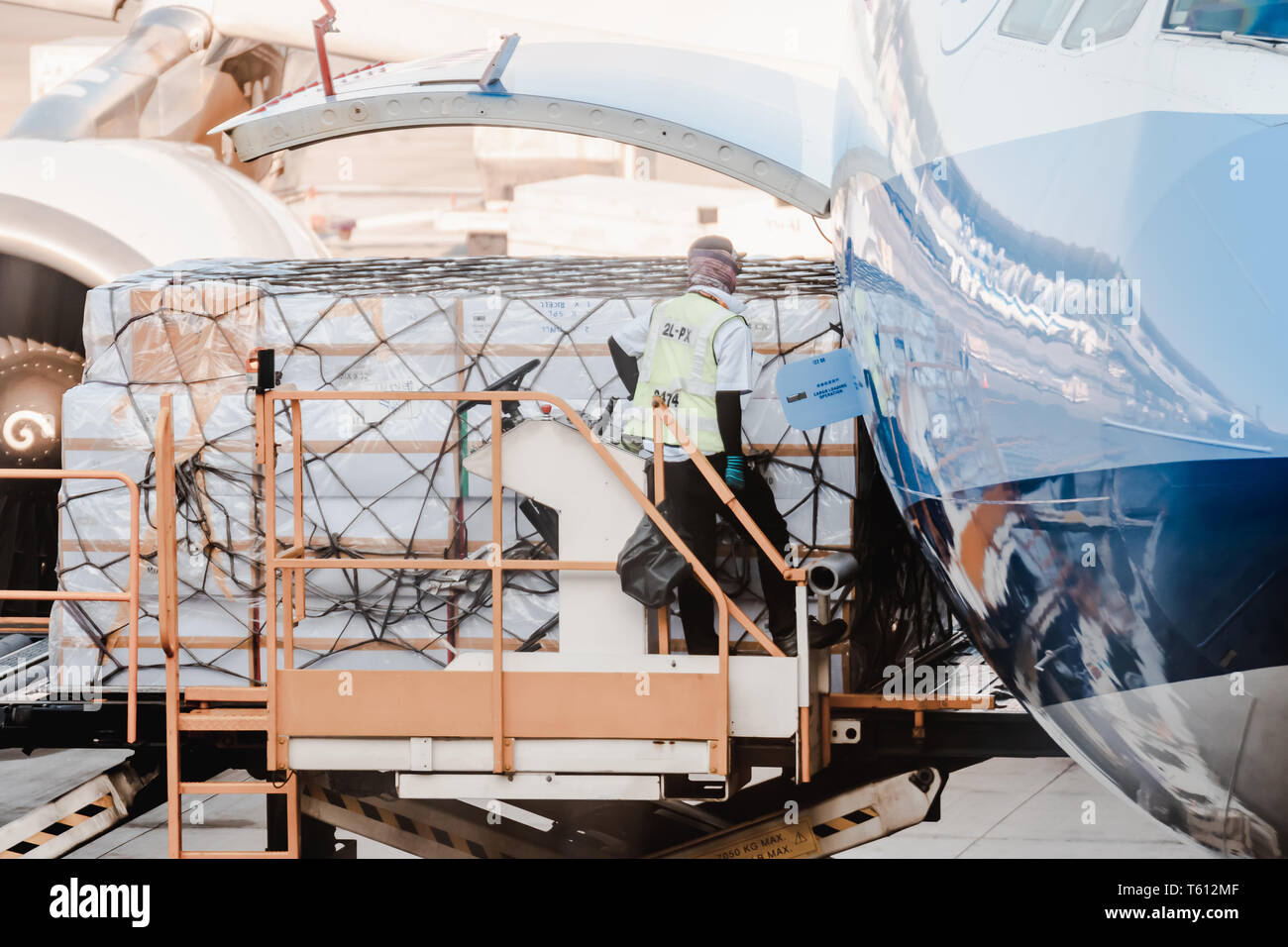 Asian ground crew using conveyor belt to load passenger luggage, cargo ...