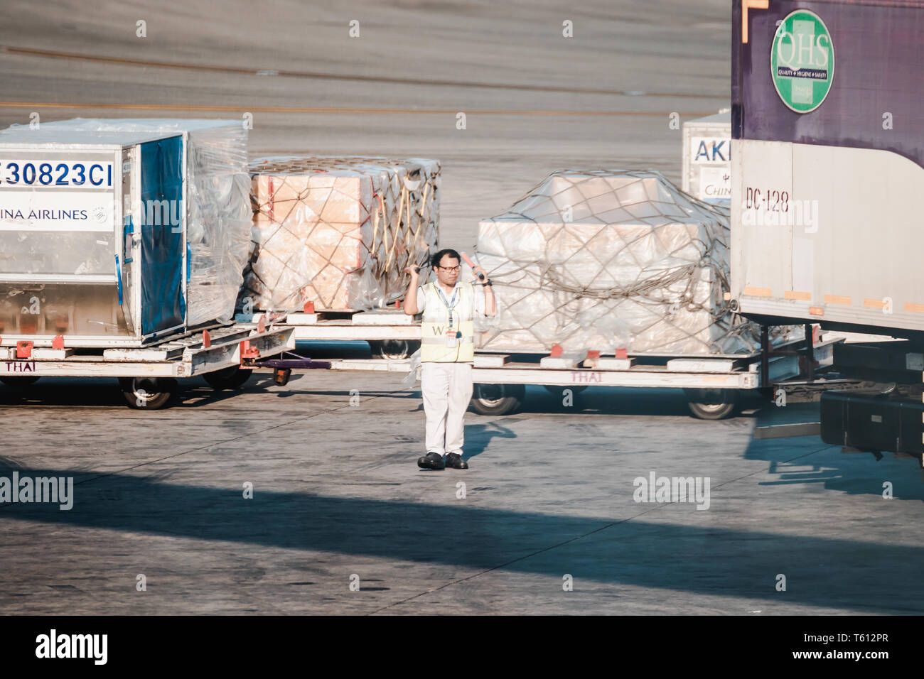 Asian ground crew using red signal wand to signal a cargo container ...