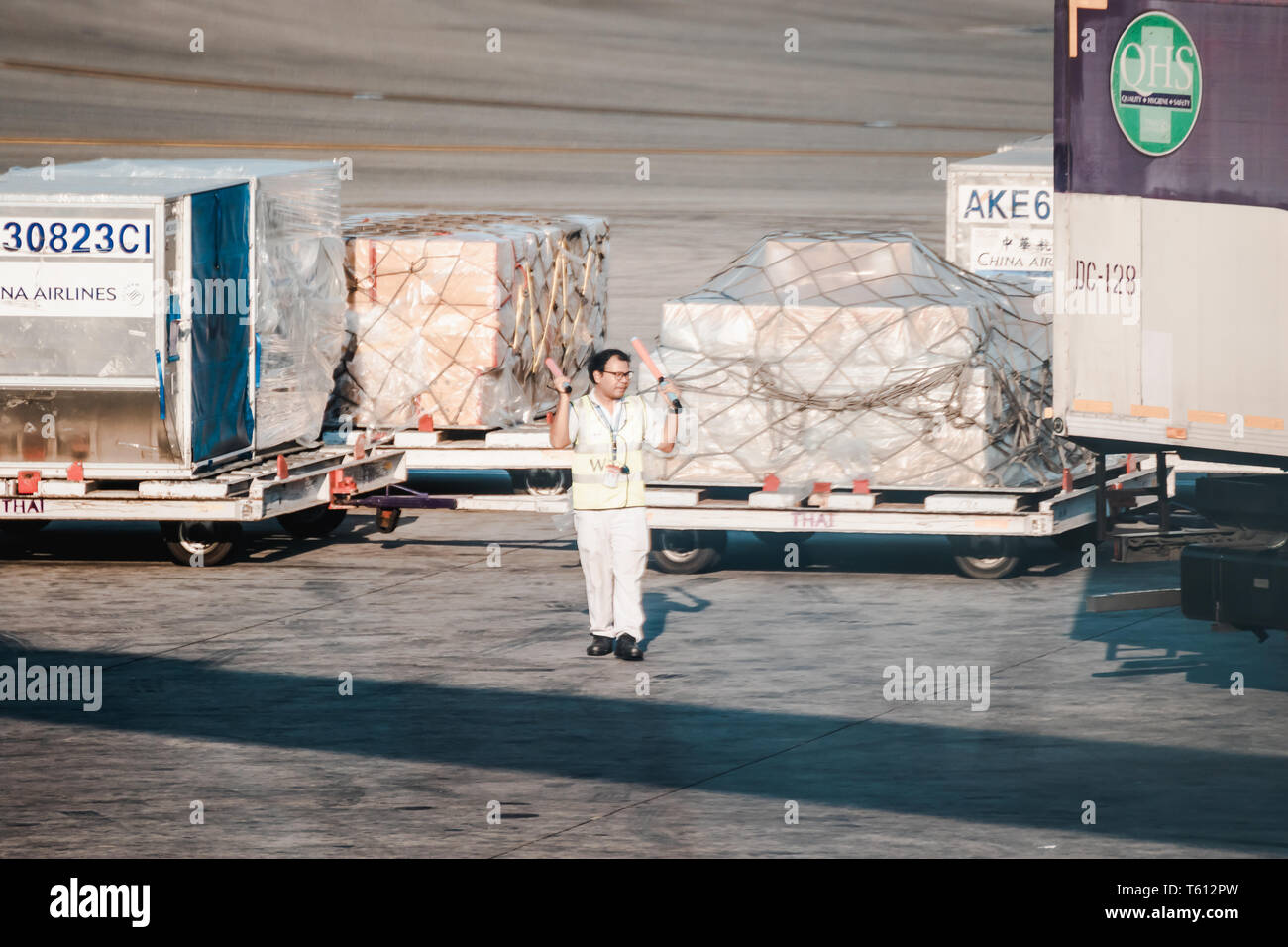 Asian ground crew using red signal wand to signal a cargo container ...