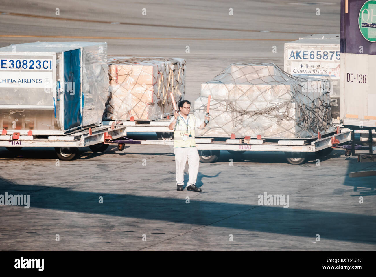 Asian ground crew using red signal wand to signal a cargo container ...