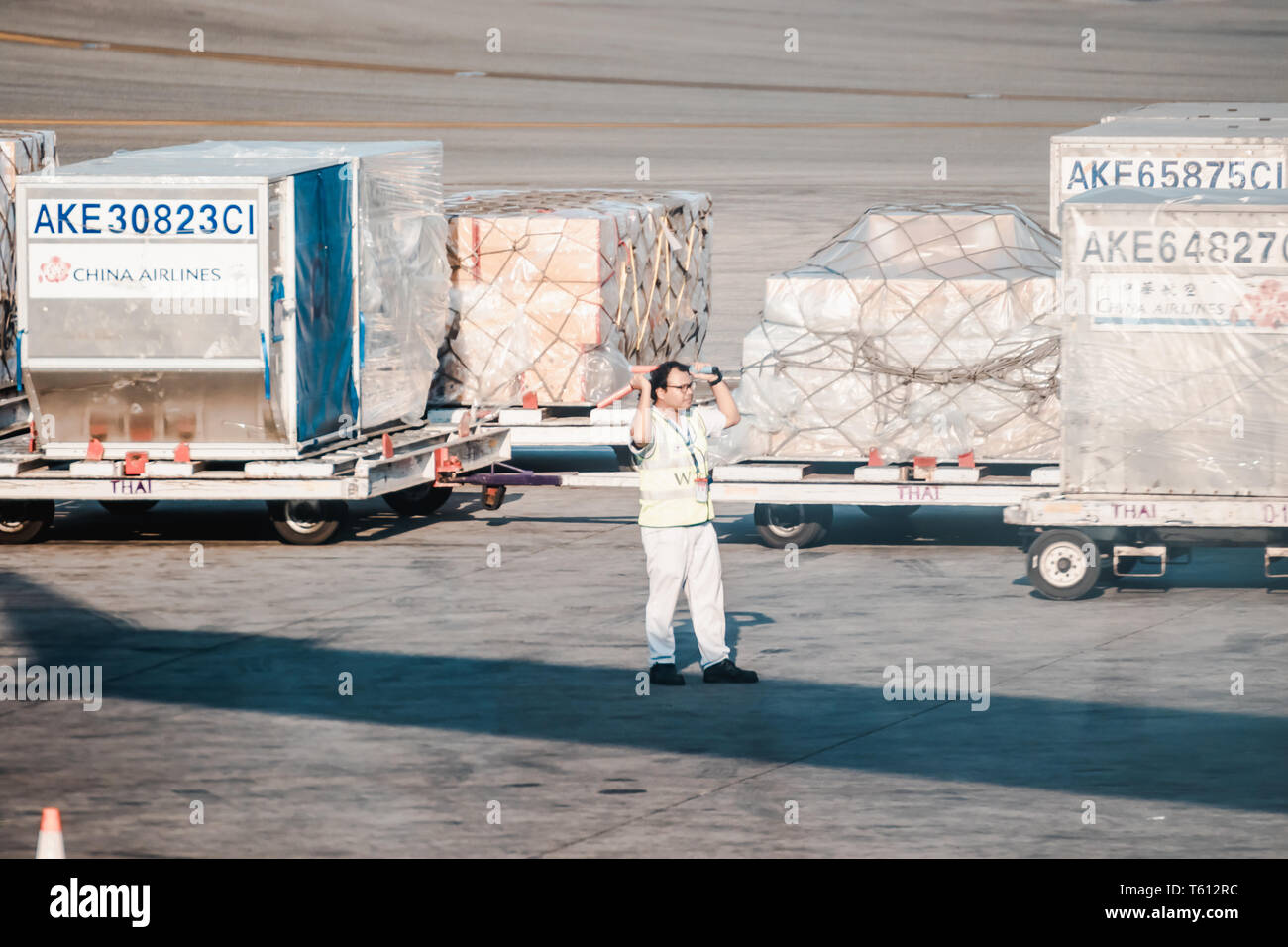 Asian ground crew using red signal wand to signal a cargo container ...