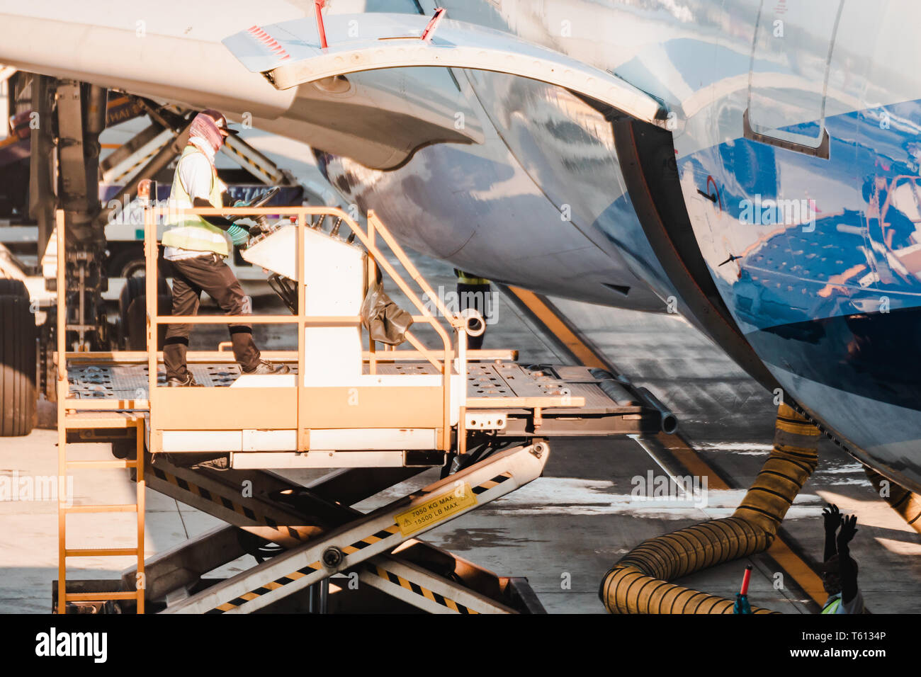 Asian ground crew raising elevated conveyor belt to load cargo into the ...
