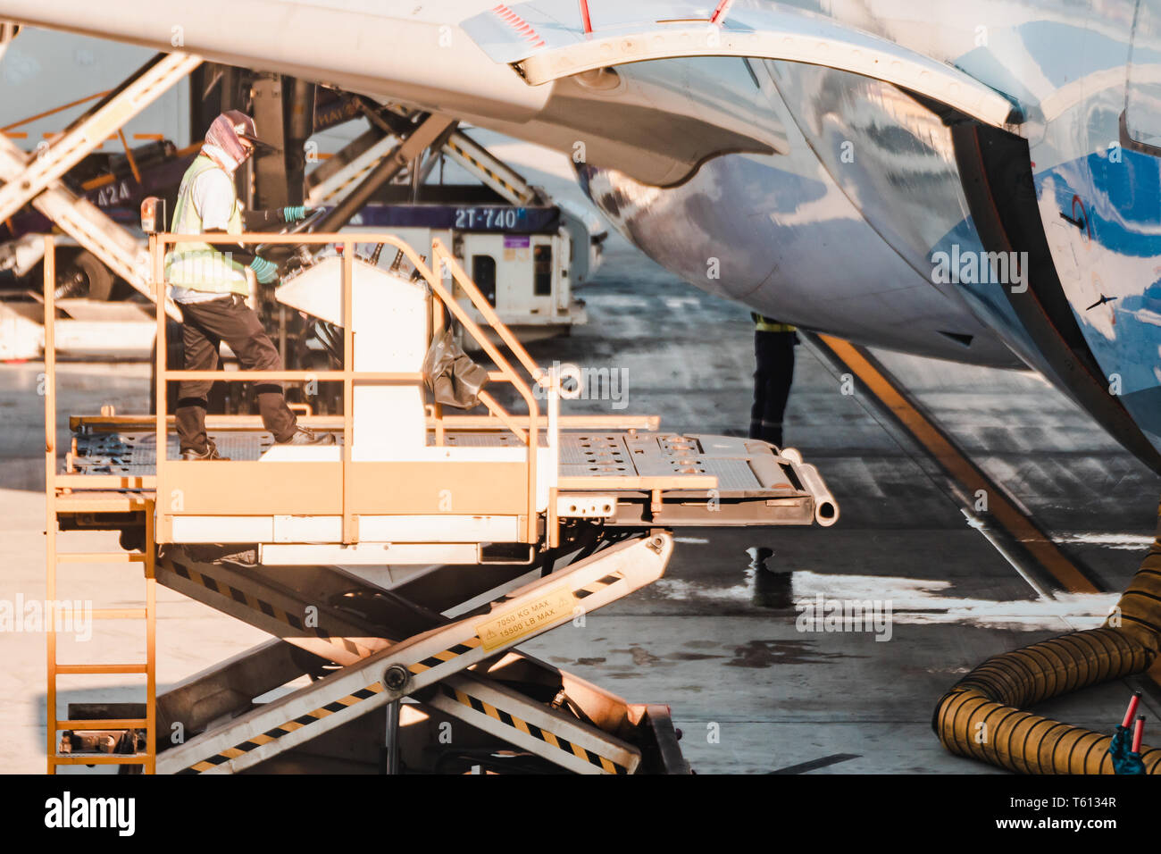Asian ground crew raising elevated conveyor belt to load cargo into the ...