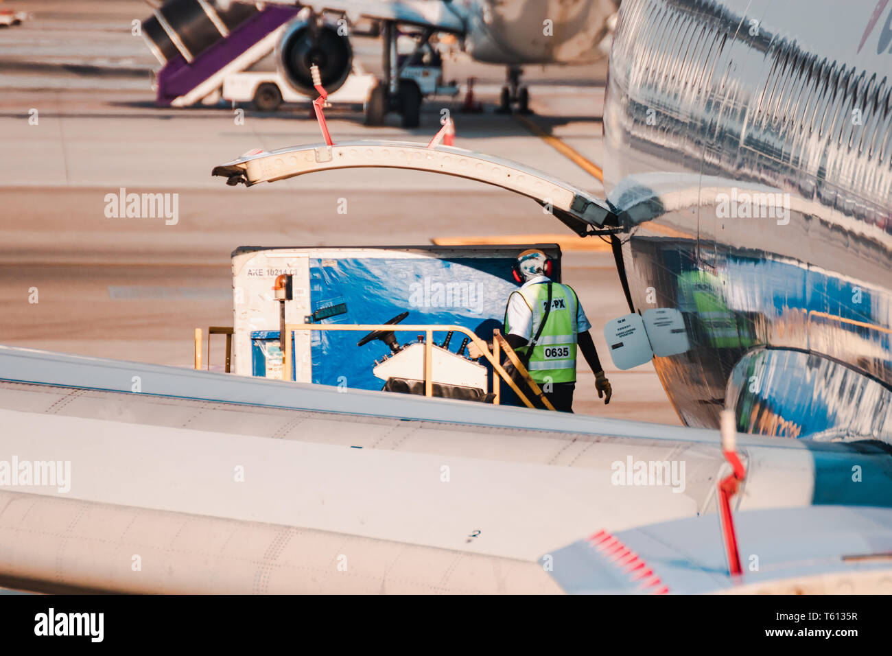 Asian ground crew using conveyor belt to load passenger luggage, cargo ...