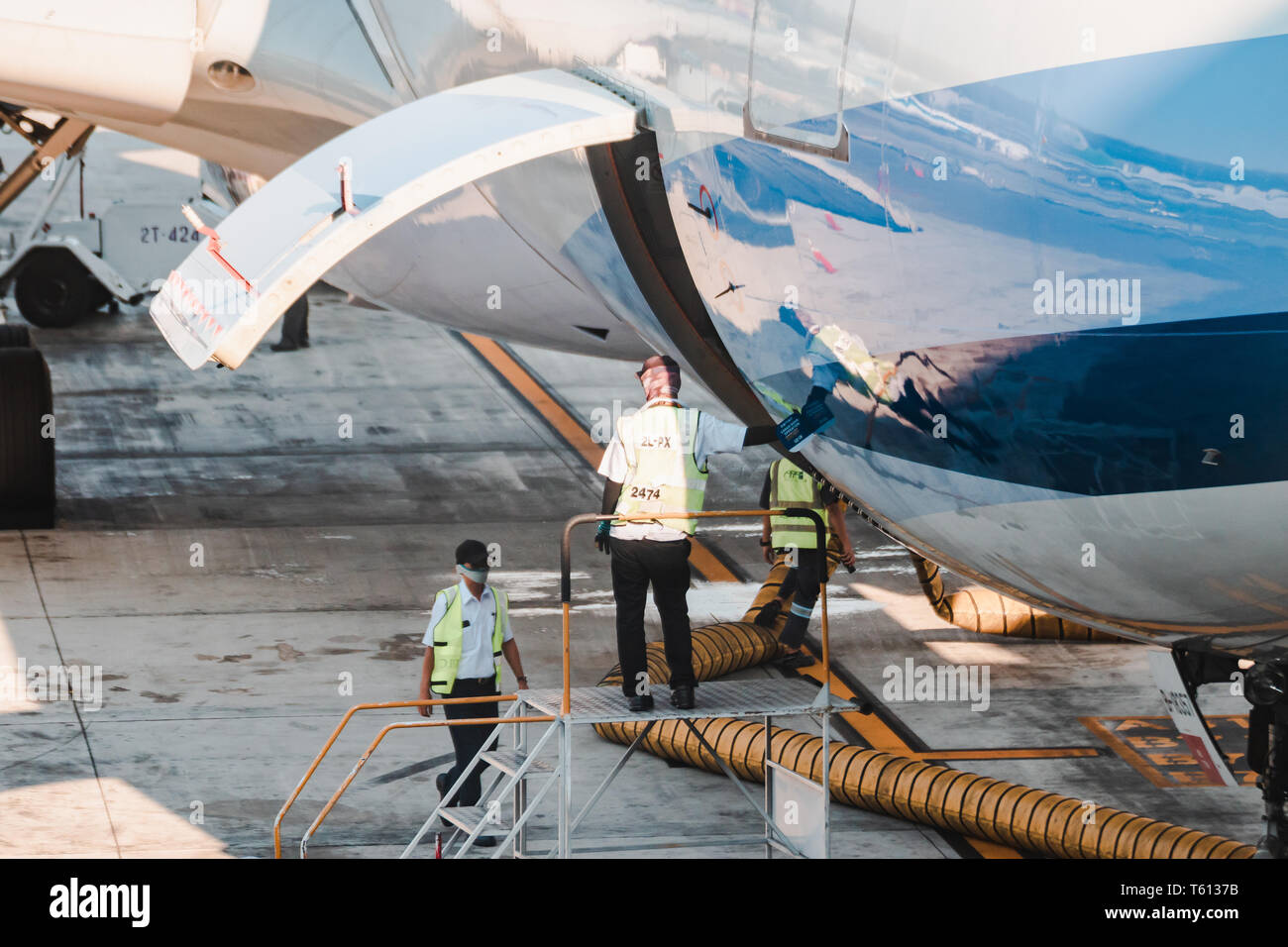 Asian ground crew opening front cargo door to load cargo, mail, and ...