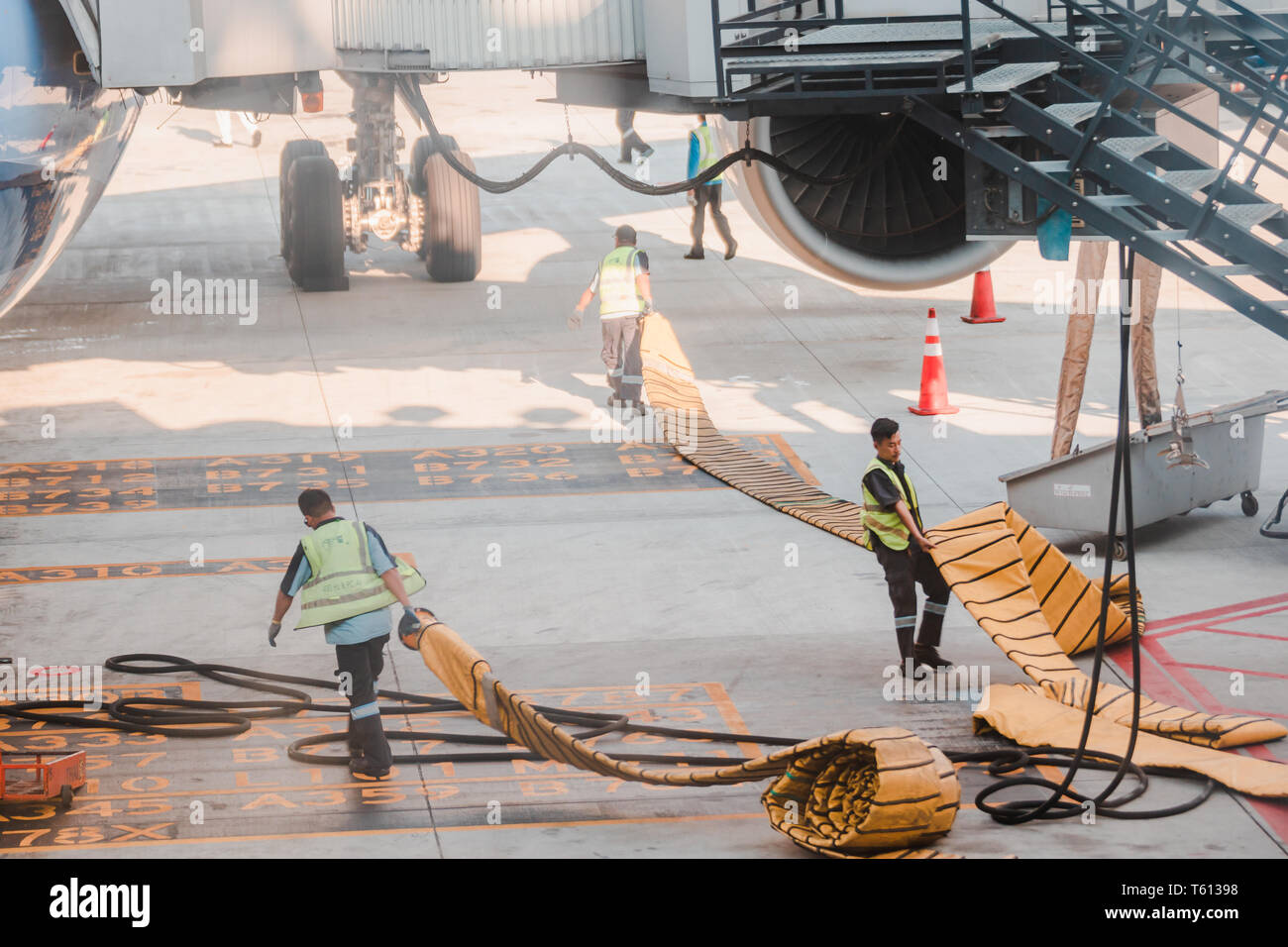 Asian ground crew carrying yellow air conditioning ventilation pipe to ...