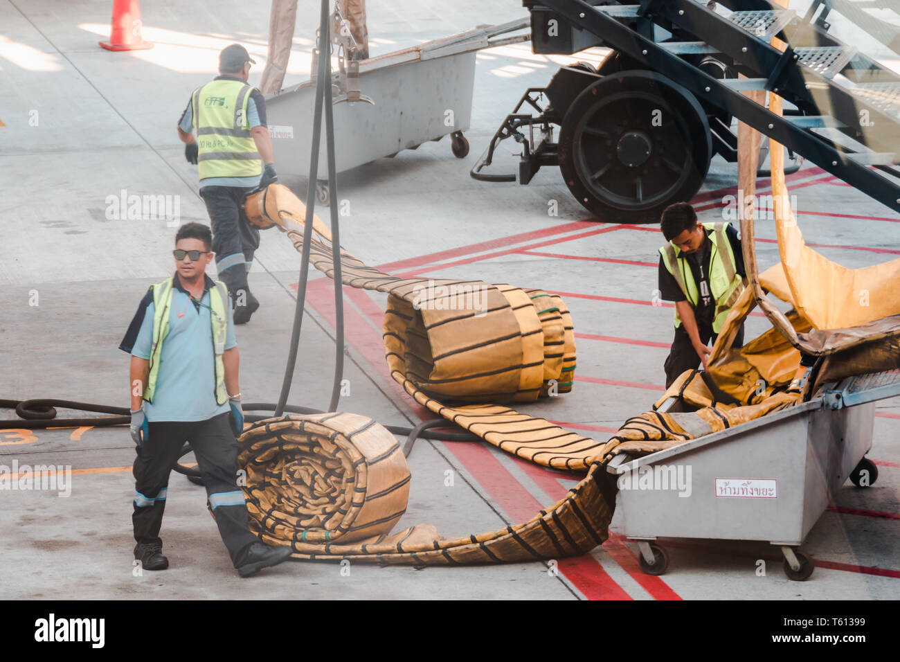 Asian ground crew carrying yellow air conditioning ventilation pipe to ...