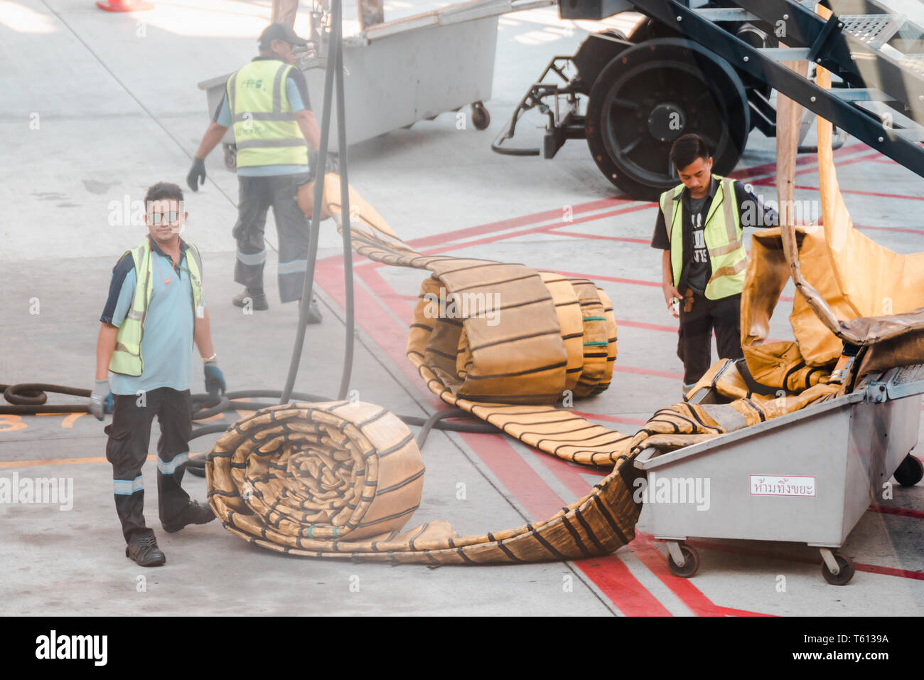 Asian ground crew carrying yellow air conditioning ventilation pipe to ...