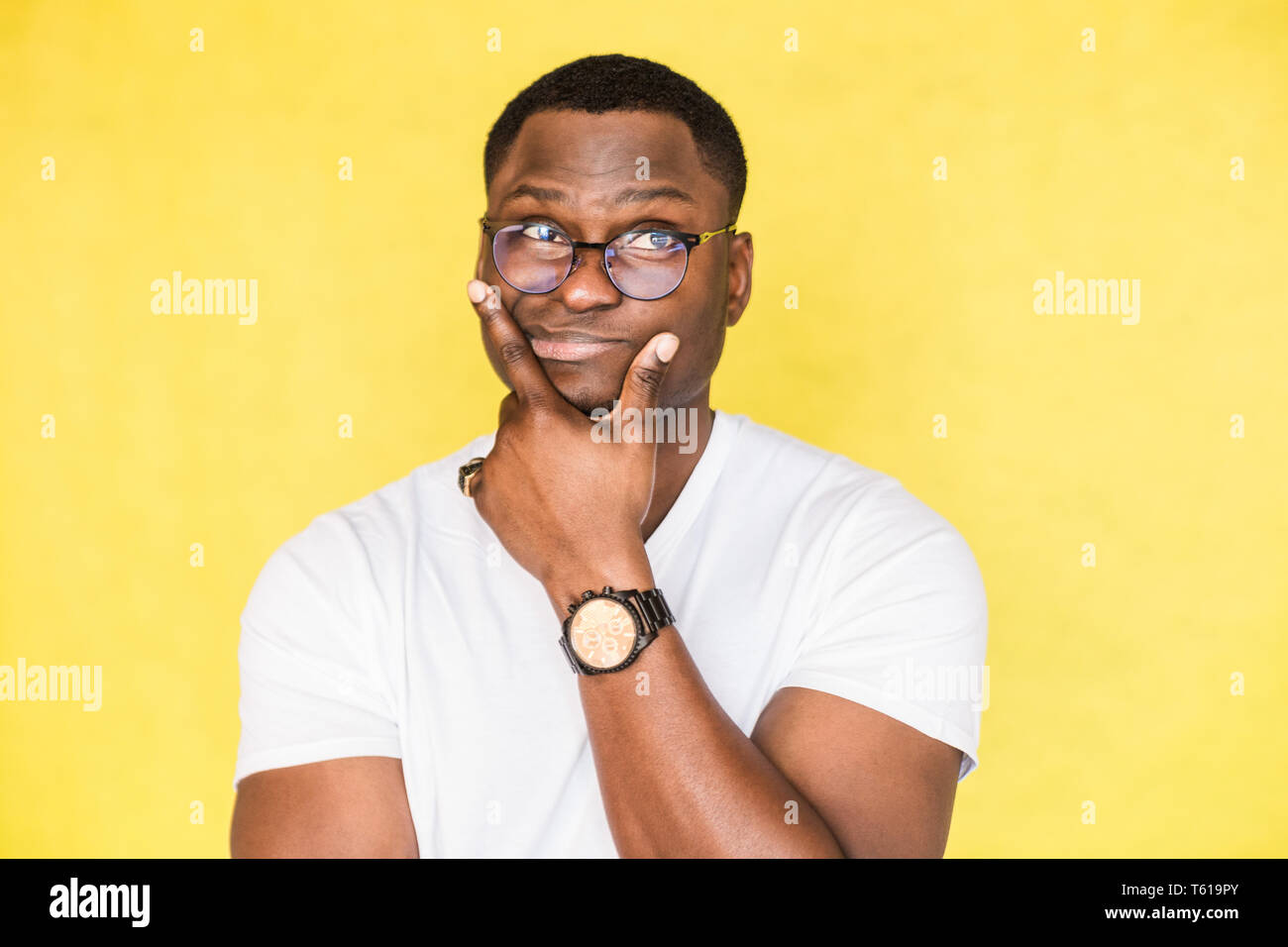 Embarrassed unsure African American man with glasses holds his chin and ...