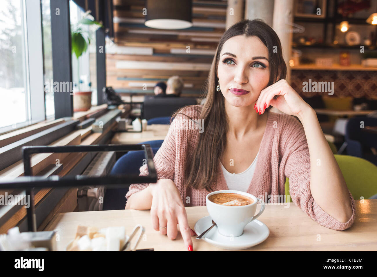 Beautiful young woman sits at a table in a cafe with a cup of coffee ...