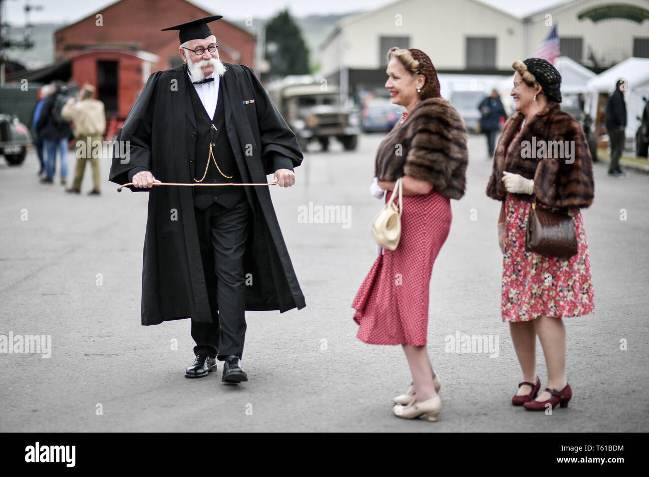 A man dressed in period clothing as a headmaster passes two women ...