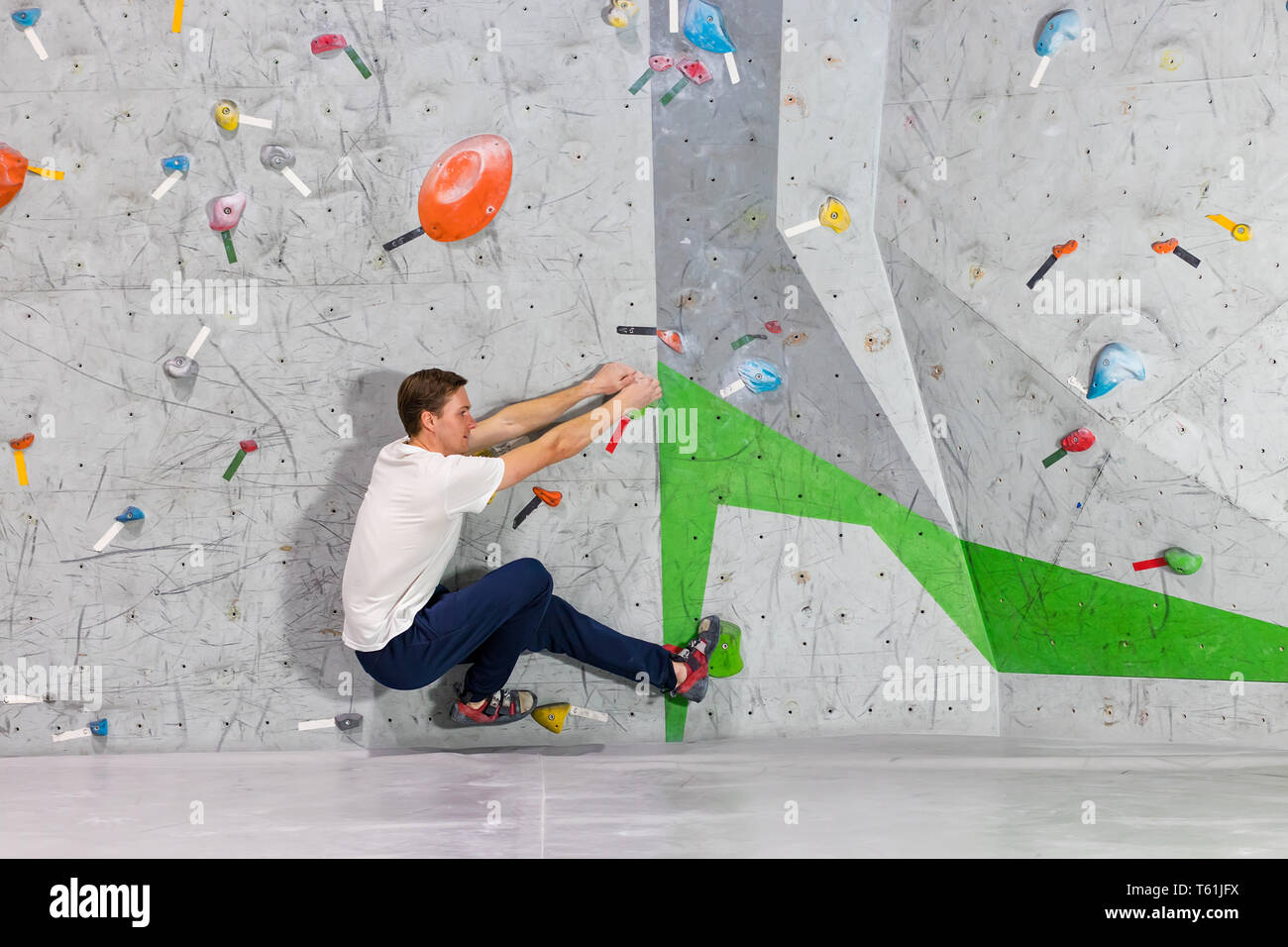 Rock climber man hanging on a bouldering climbing wall, inside on ...