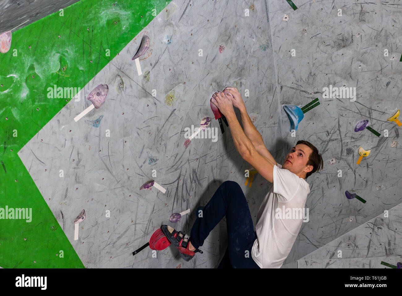 Rock climber man hanging on a bouldering climbing wall, inside on ...