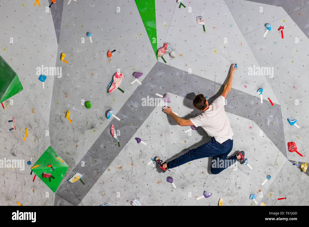 Rock climber man hanging on a bouldering climbing wall, inside on ...