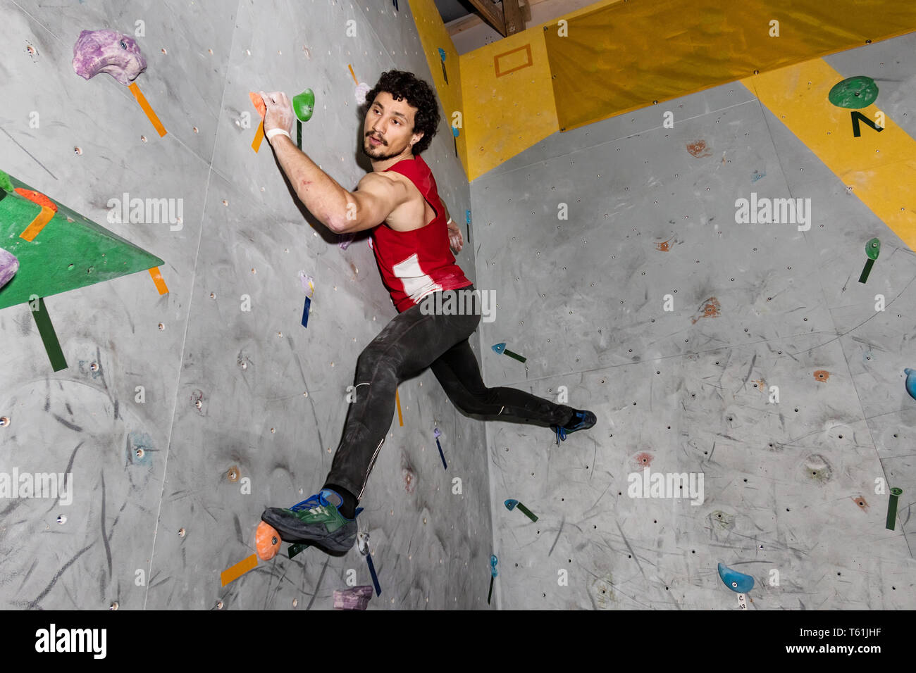 Rock climber man hanging on a bouldering climbing wall, inside on ...