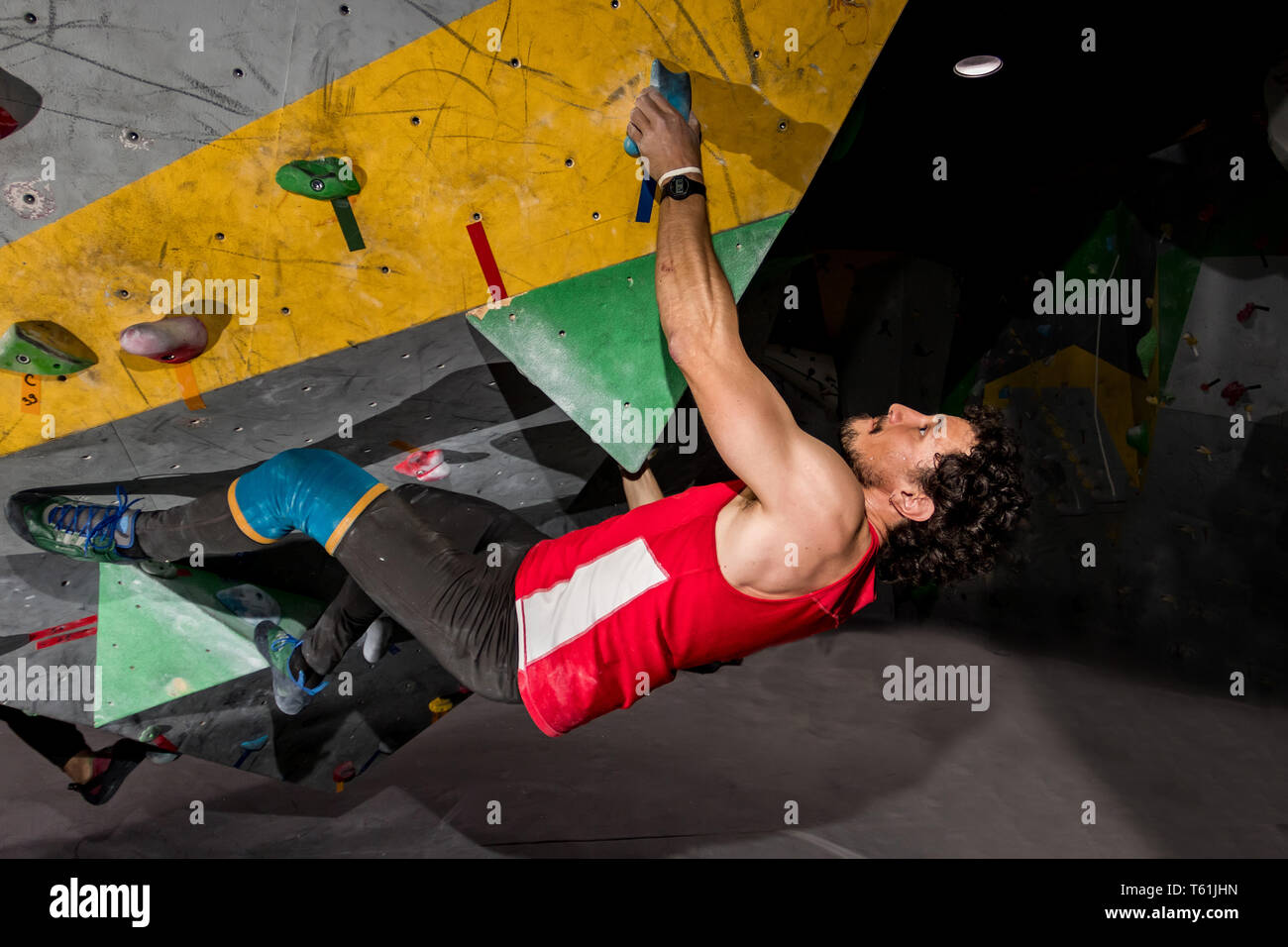 Rock climber man hanging on a bouldering climbing wall, inside on ...