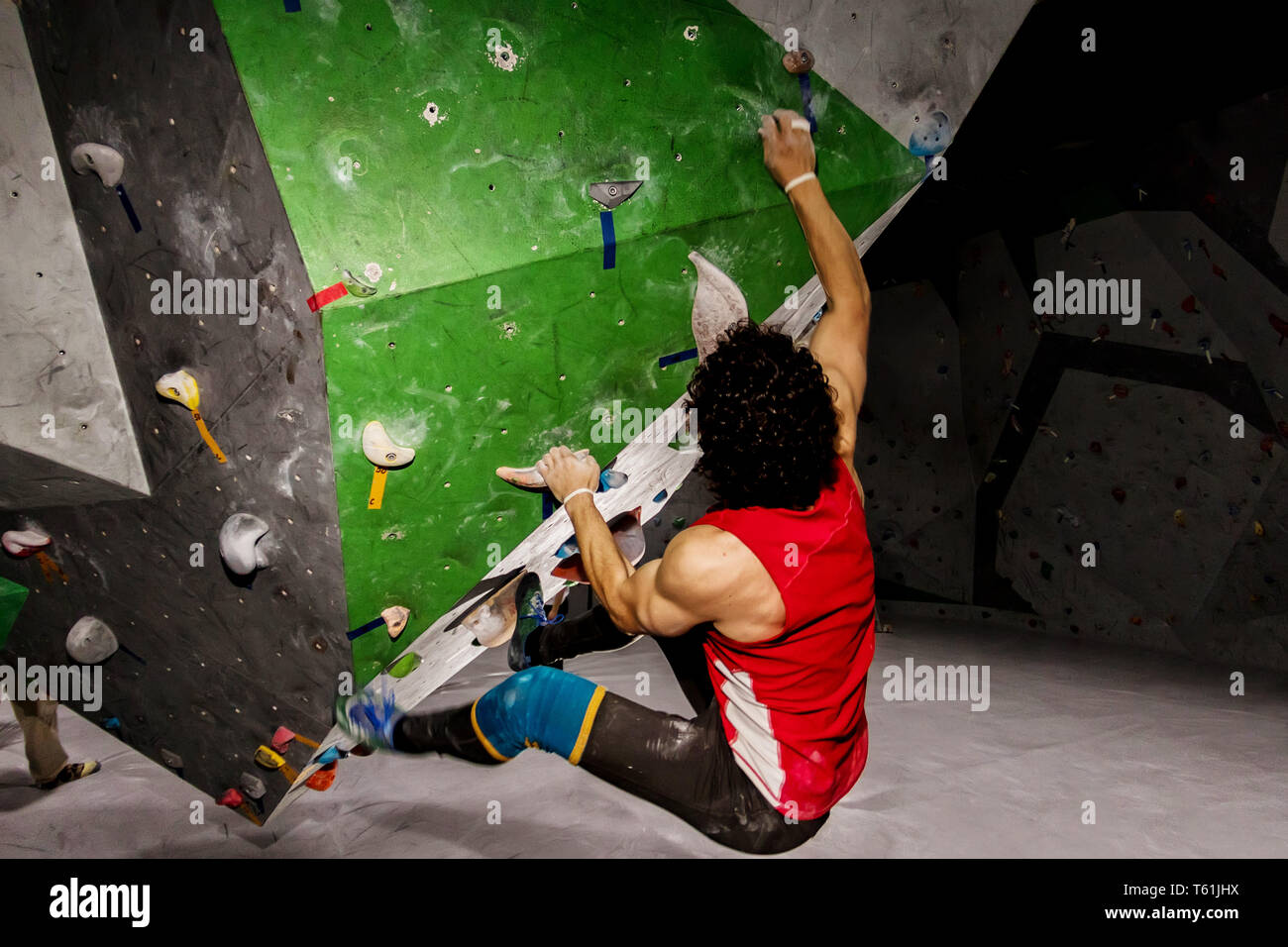 Rock climber man hanging on a bouldering climbing wall, inside on ...