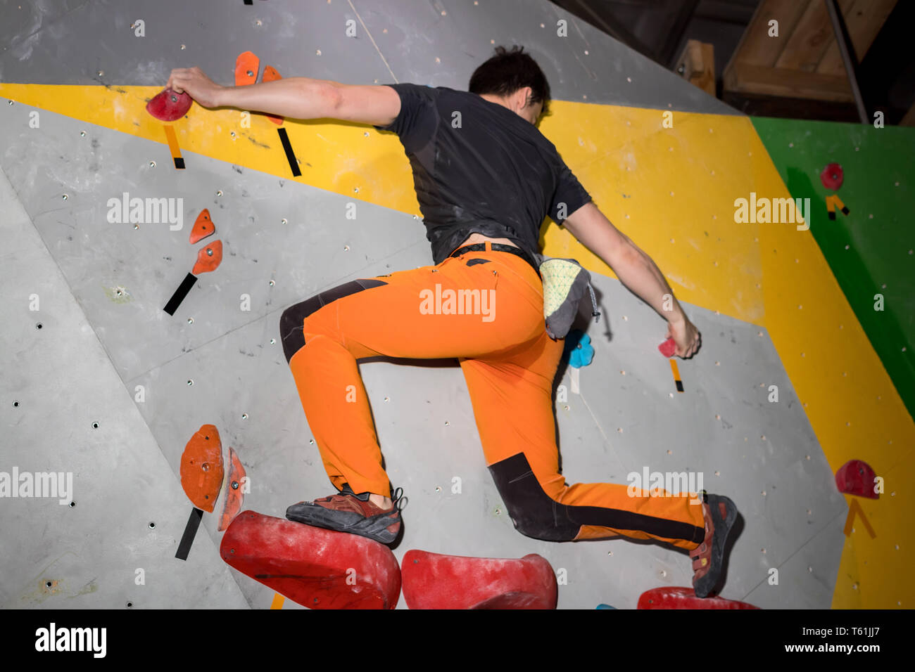 Rock climber man hanging on a bouldering climbing wall, inside on ...