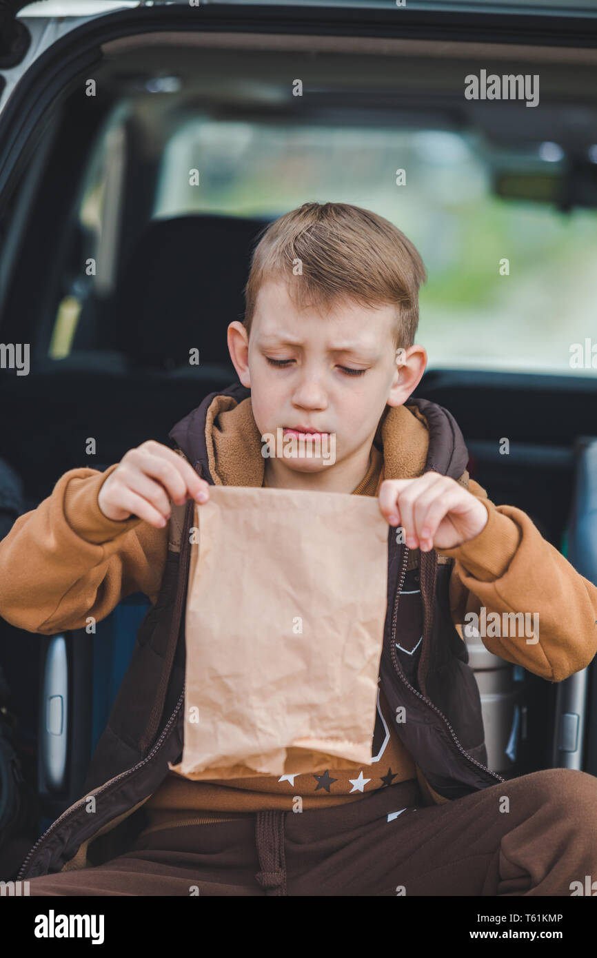 little kid looking into paper bag with candies sitting in car trunk ...