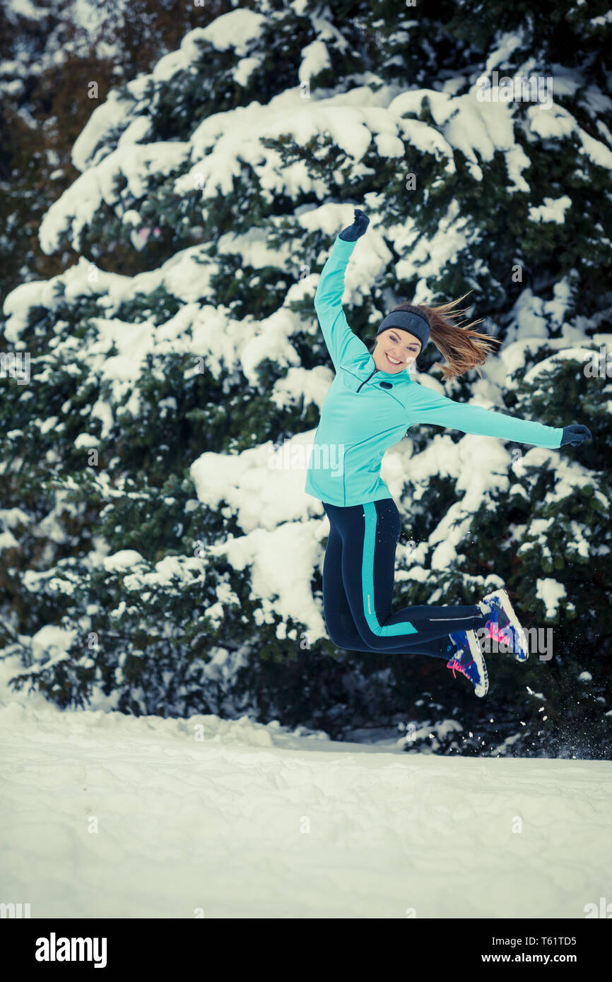 Sporty girl jumping in snow with trees in background. Winter sports ...