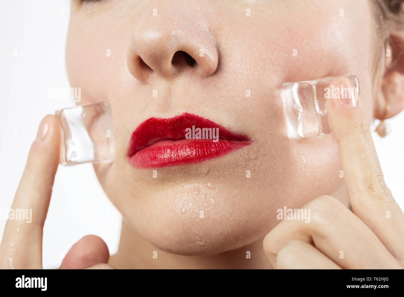 serious young woman applying ice cubes on her face skin, isolated on ...