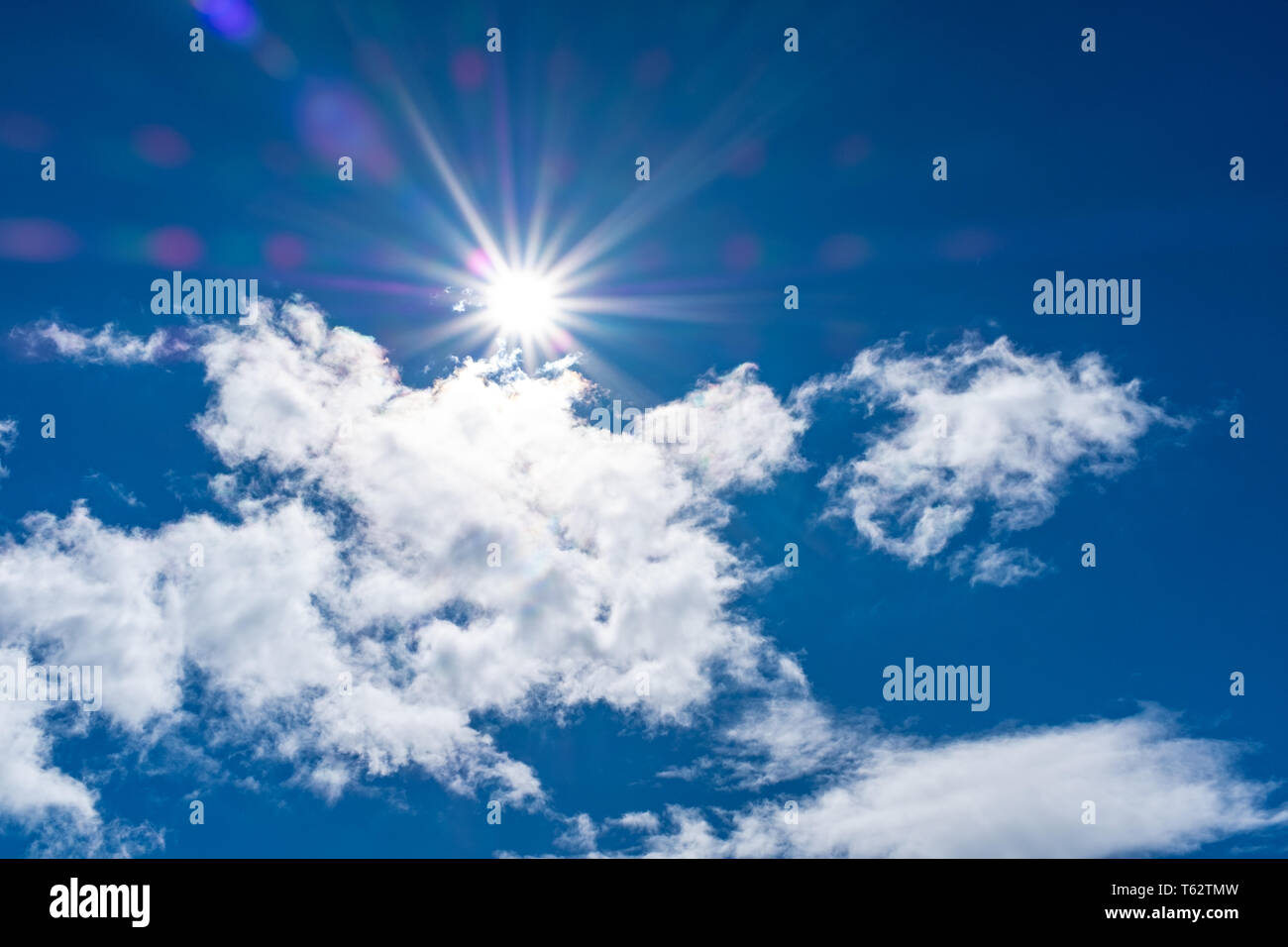Blue sky with white puffy clouds and a sun star Stock Photo - Alamy