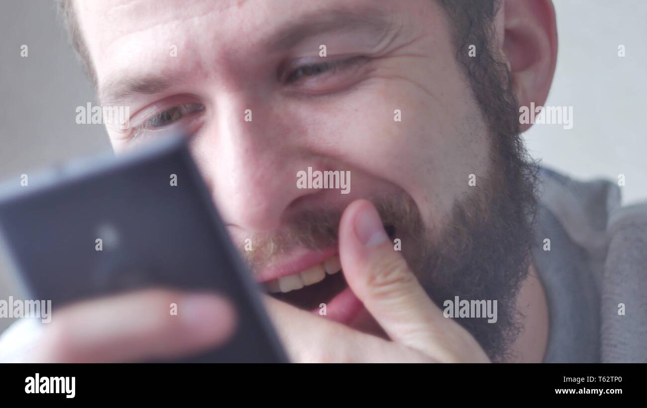A young bearded man uses his mobile phone. Close-up shot, focus on eyes ...