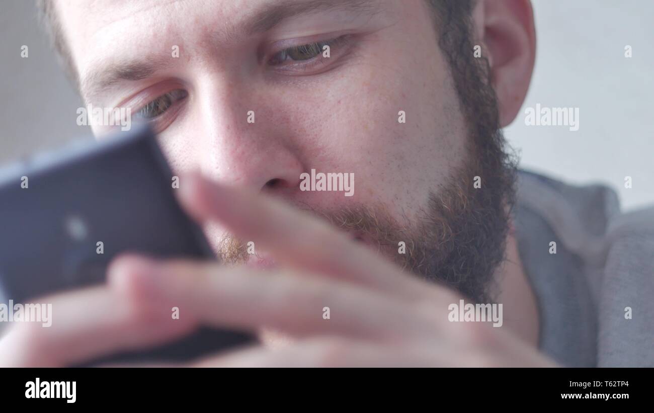 A young bearded man uses his mobile phone. Close-up shot, focus on eyes ...