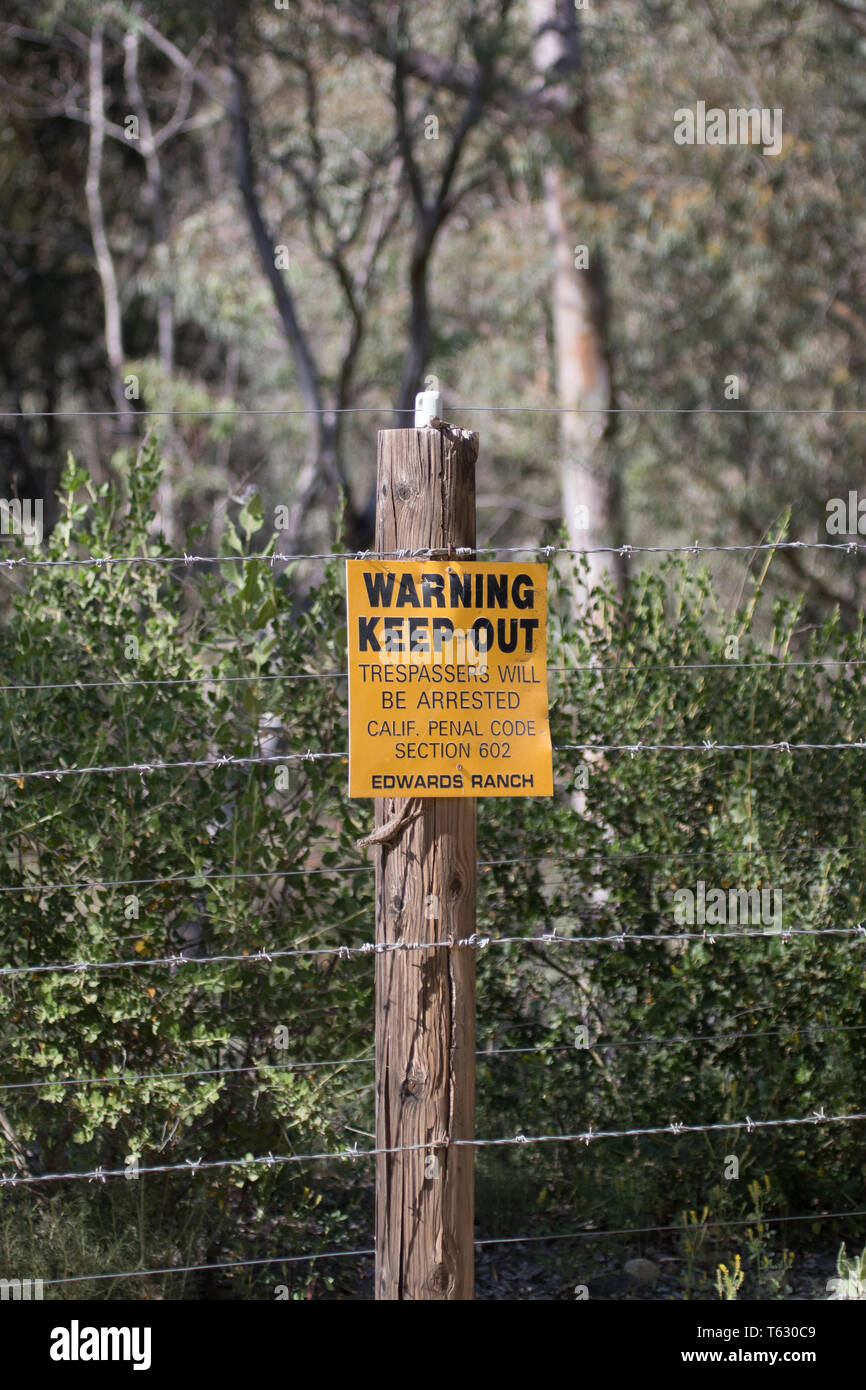 Warning keep out sign and barbed wire fence attached to a wooden post ...