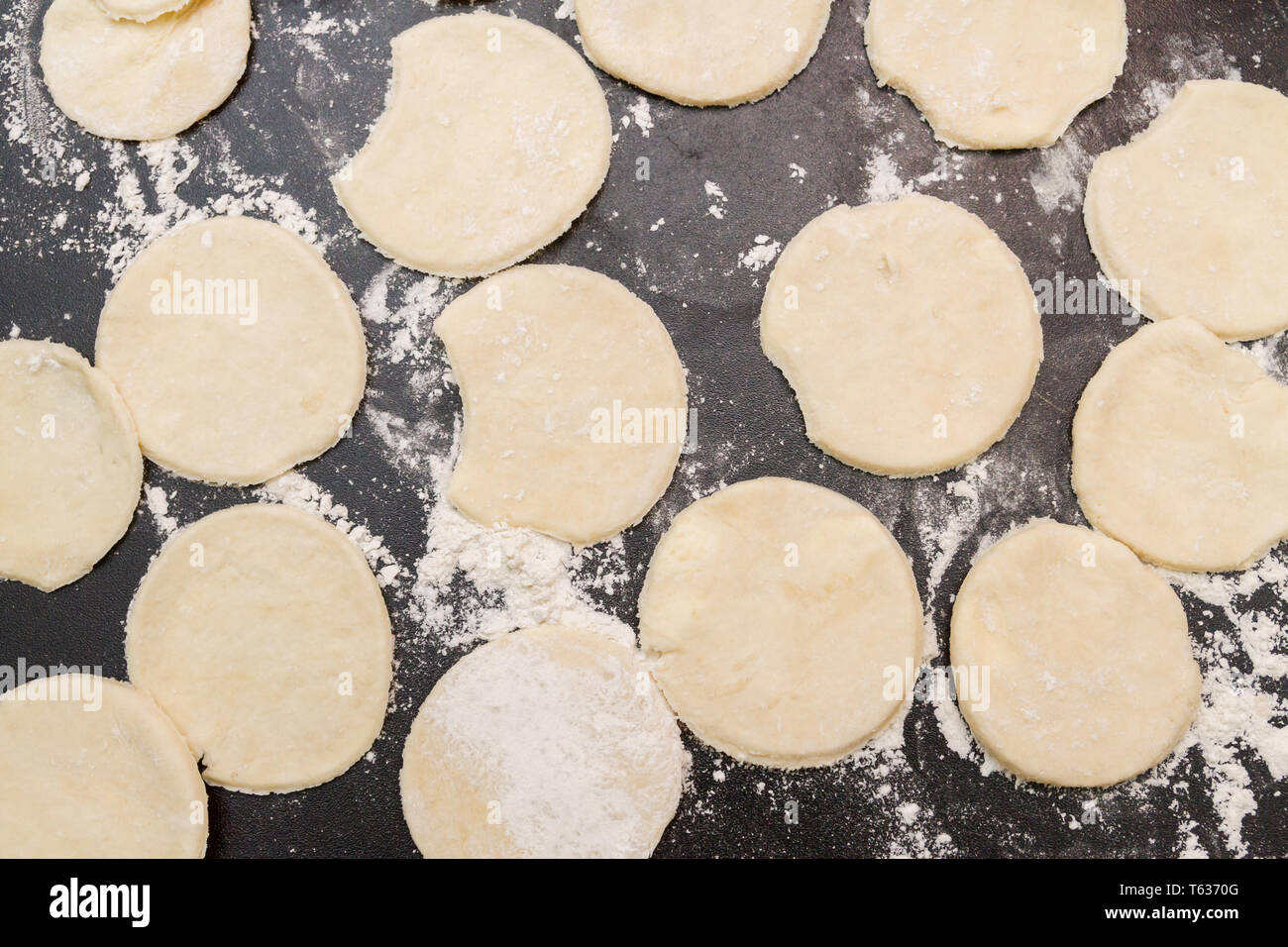Rolled out raw dough cut into roundels on a table with scattered flour ...