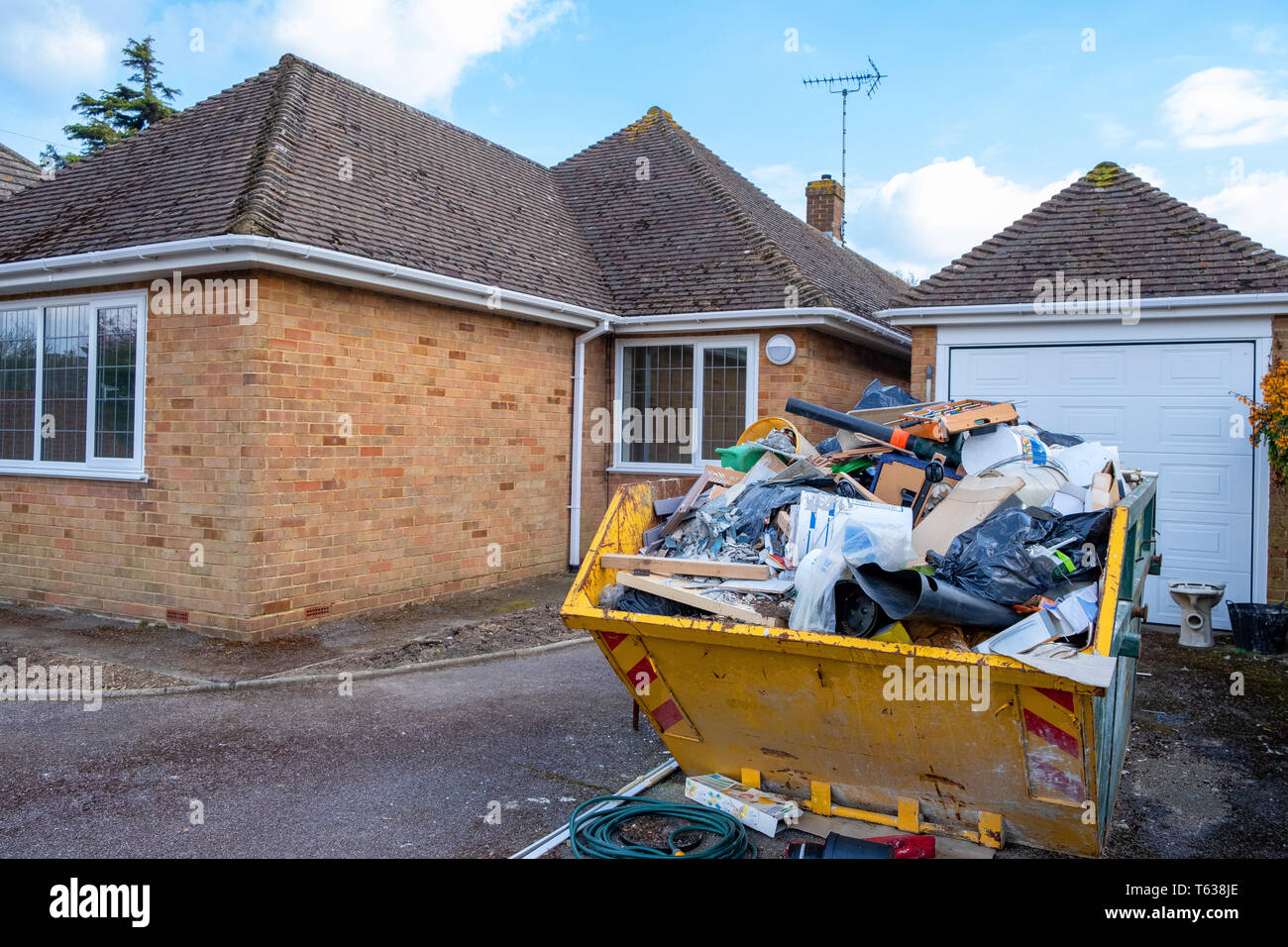 A full yellow rubbish skip on a house driveway Stock Photo - Alamy