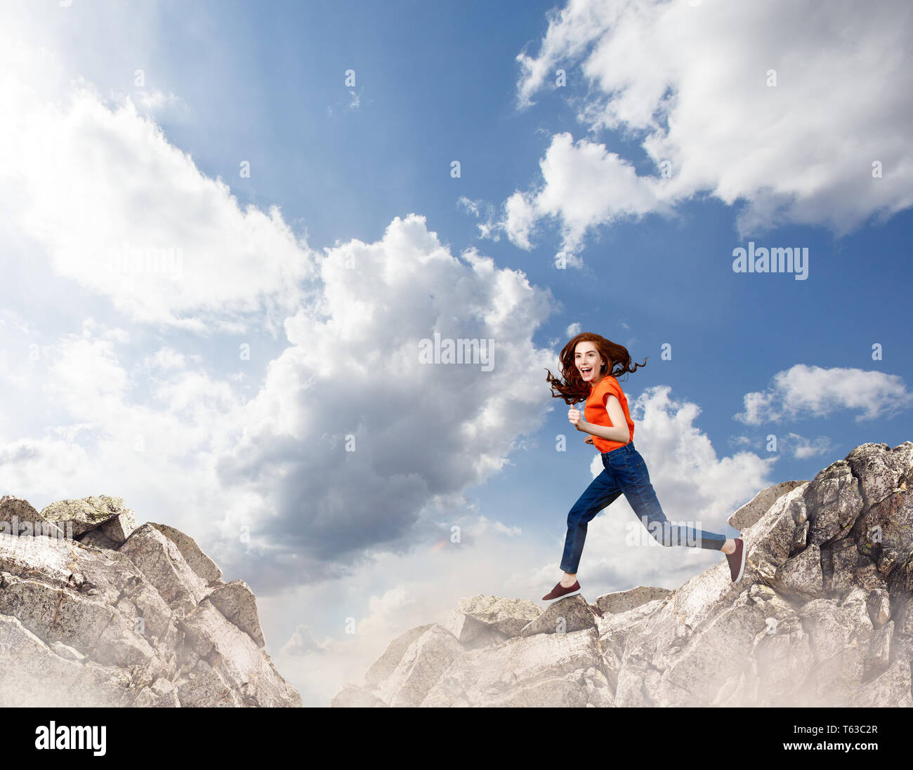 Redhead woman jumps over cliff on blue sky background Stock Photo - Alamy