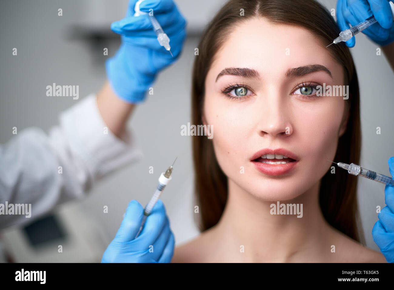 Hands of beauticians holding syringes around doll like woman face ready ...