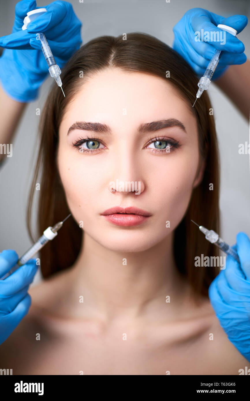 Hands of beauticians holding syringes around doll like woman face ready ...