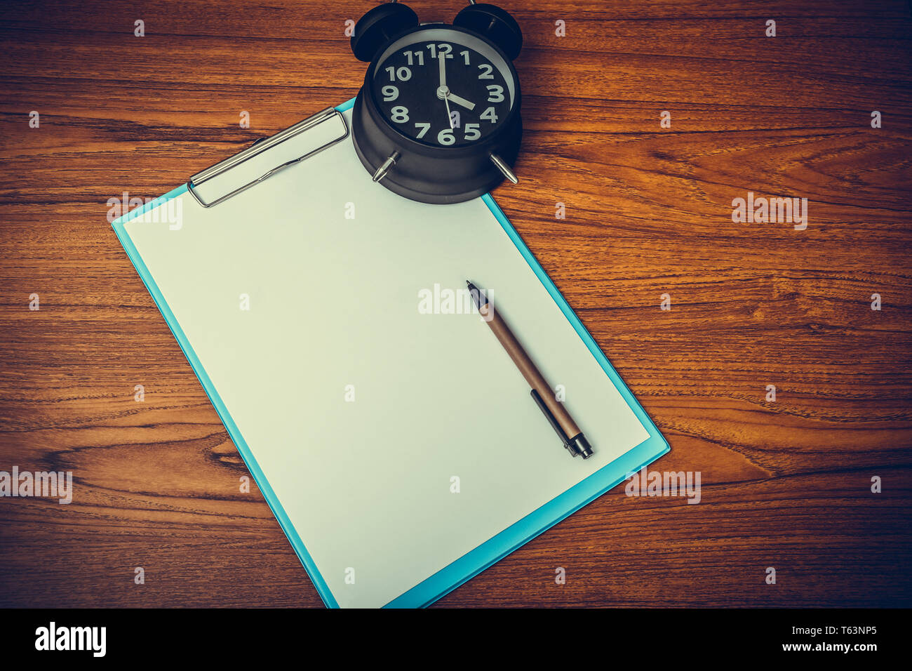 Black vintage alarm clock with clipboard and blank white paper and pen ...