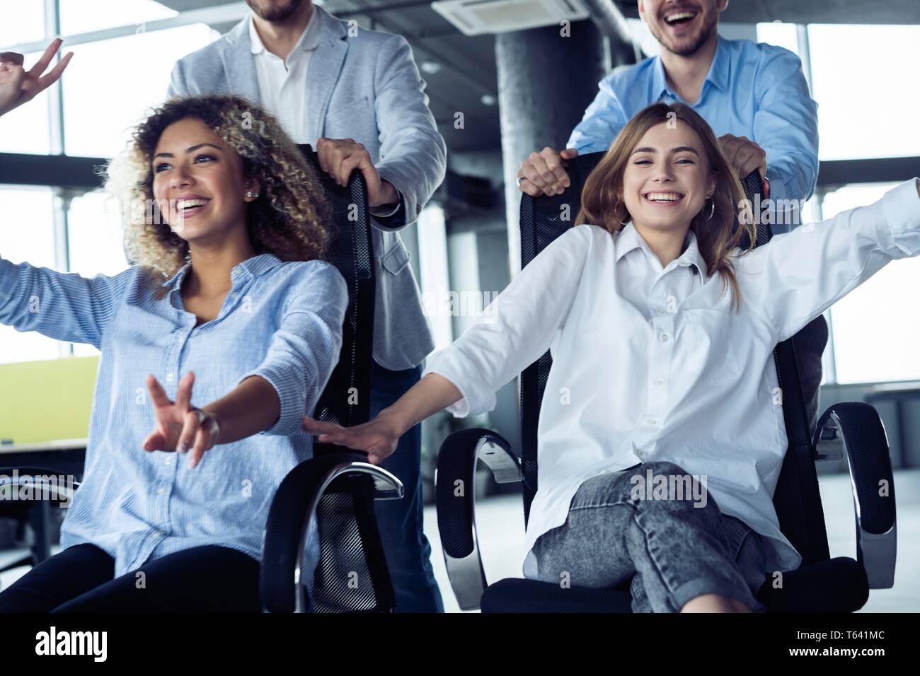 Positive colleagues having fun with office chairs Stock Photo - Alamy