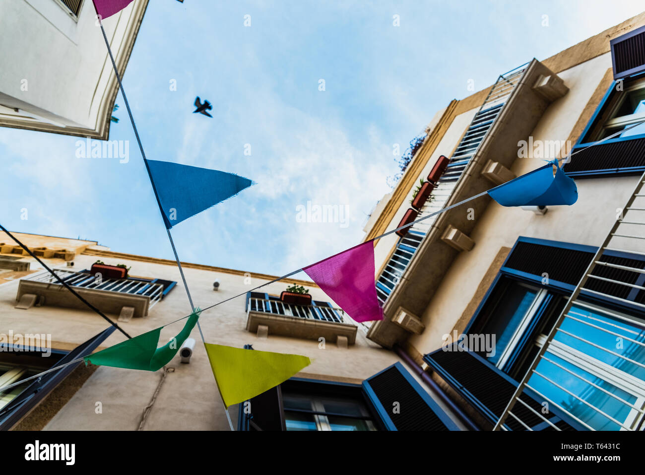 Colorful pennants seen from below crossing a street with old buildings ...