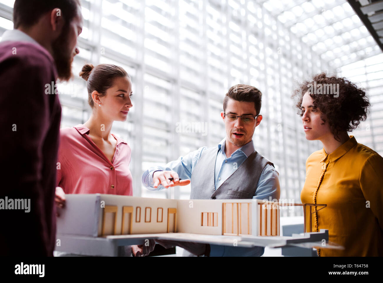 A group of young architects with model of a house standing in office ...