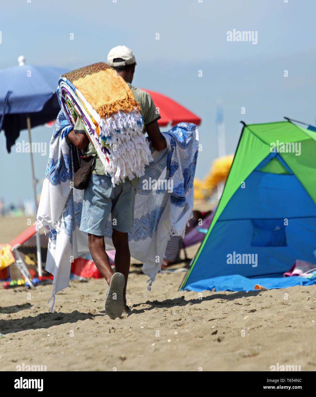 street vendor walks on the beach to sell the many rugs he carries on ...